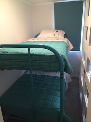 Uma cama beliche com estrutura e roupa de cama verde, uma janela com vista e uma porta com espelho.