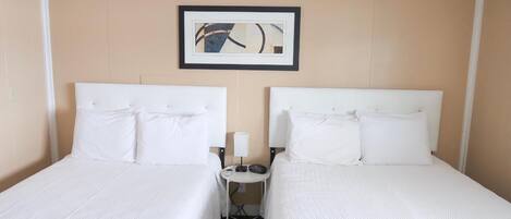 Quarto de hotel com duas camas, uma mesa pequena com abajur e um quadro abstrato emoldurado na parede.