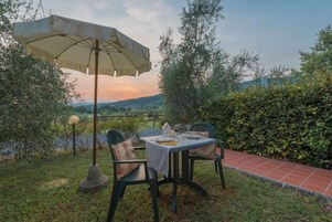 Uma área de refeições ao ar livre com mesa, cadeiras, guarda-sol e vista para a paisagem.