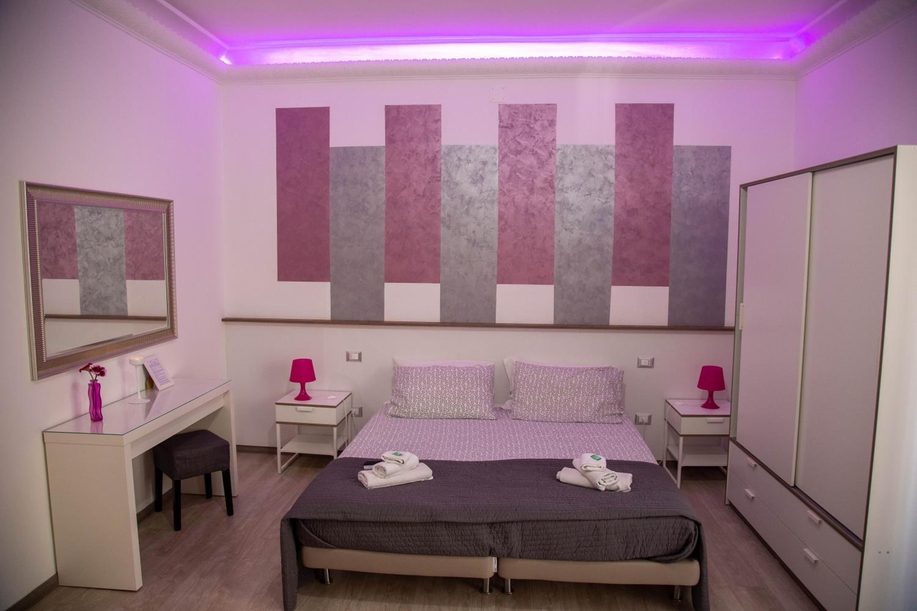 Quarto com cama, duas mesas de cabeceira, escrivaninha, cadeira, guarda-roupa e uma grande pintura abstrata na parede.
