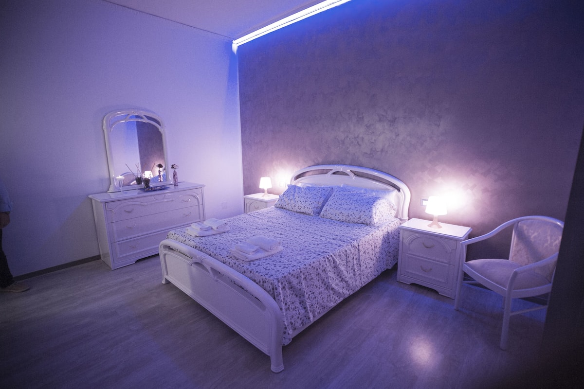 Quarto com cama, penteadeira, cadeira e abajures de cabeceira.
