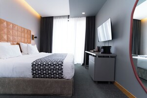Quarto de hotel com cama, escrivaninha, televisão e um espelho grande.
