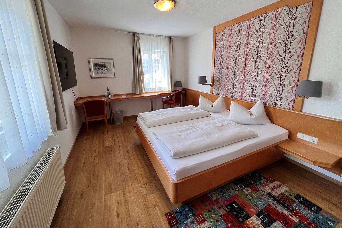 Quarto de hotel com cama, escrivaninha, cadeira, televisão e parede estampada.