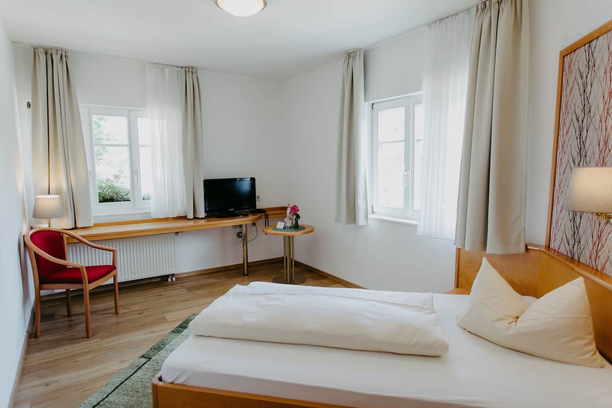 Quarto de hotel com uma cama, uma escrivaninha com televisão, uma cadeira e uma janela.