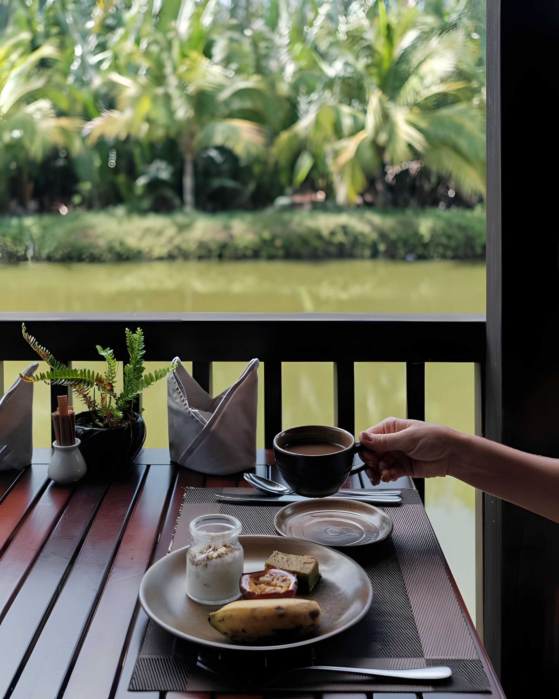 Uma mesa de jantar com uma banana, uma tigela de sobremesa, uma xícara de café e uma planta.