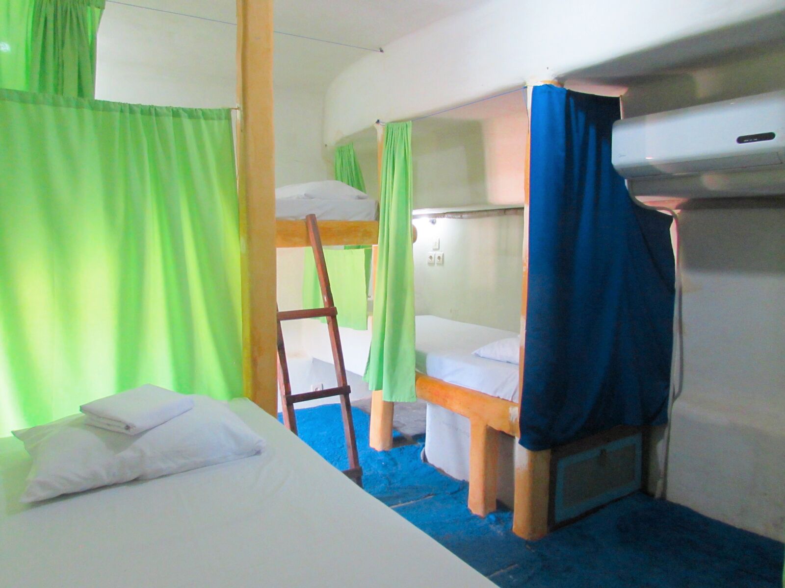 Quarto com beliche, uma cama branca e cortinas verdes.