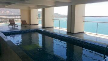 Piscina interna com vista para o mar e montanhas.