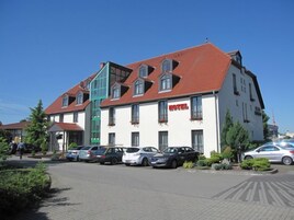Um hotel com telhado vermelho e paredes brancas, um estacionamento com vários carros e um céu azul límpido.