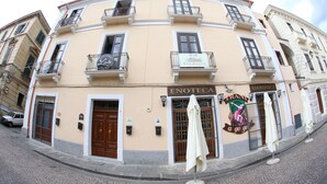 Um edifício com várias varandas, um letreiro com 'ENOTECA' e guarda-sóis.