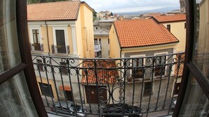 Vista de uma varanda com telhado de azulejos, guarda-corpo de metal e céu claro.