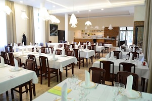 Um restaurante amplo com várias mesas preparadas para refeições, com toalhas de mesa brancas e cadeiras de madeira.