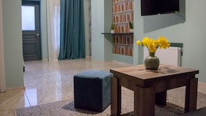 Uma sala de estar moderna com uma mesa de madeira, um banquinho azul-escuro, uma estante e uma TV de tela plana fixada na parede.
