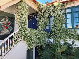 Um edifício com porta azul e janelas, coberto por trepadeiras floridas brancas.