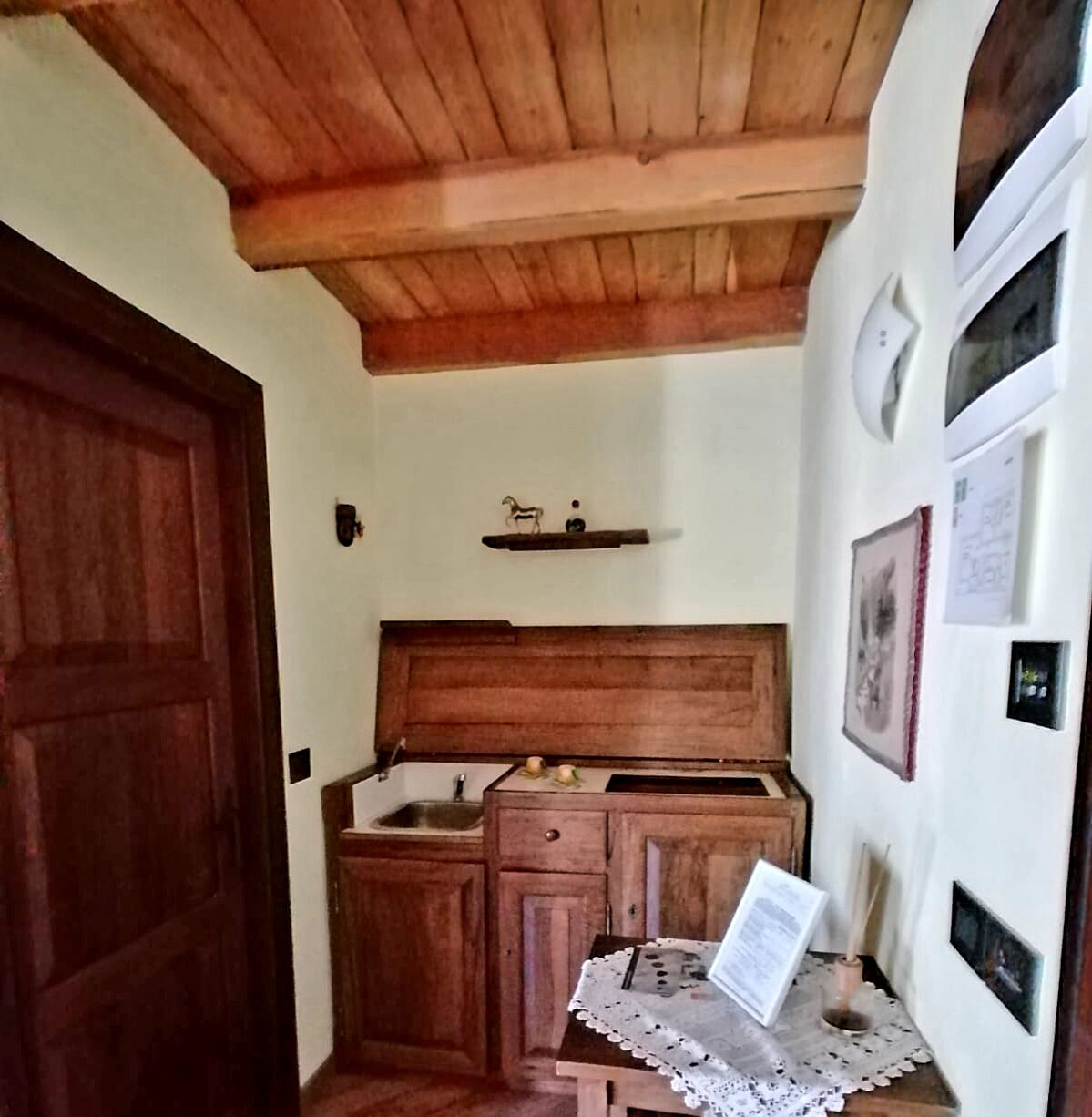 Uma cozinha compacta com armários de madeira, uma pia e uma mesa pequena com toalha de renda.