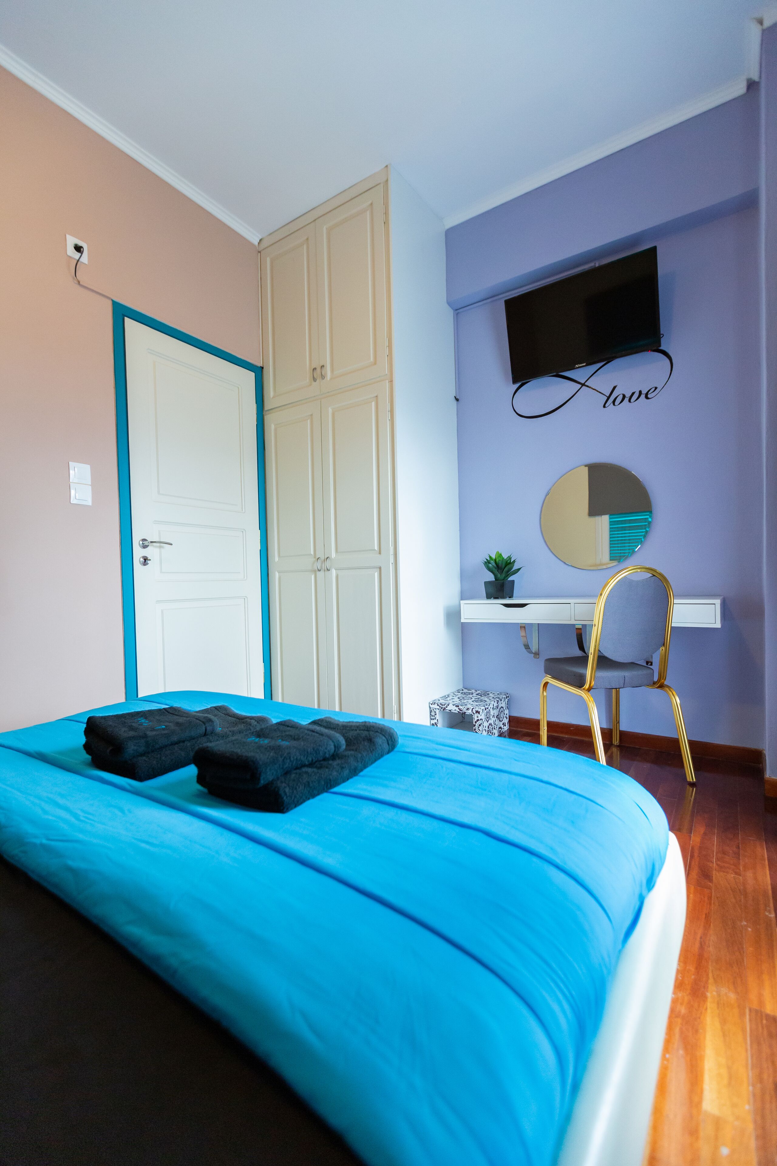 Quarto com cama, escrivaninha, cadeira, televisão e guarda-roupa.