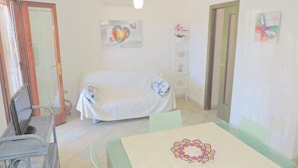 Quarto com cama, escrivaninha e cadeira. Há uma janela, uma porta e uma parede com obras de arte.