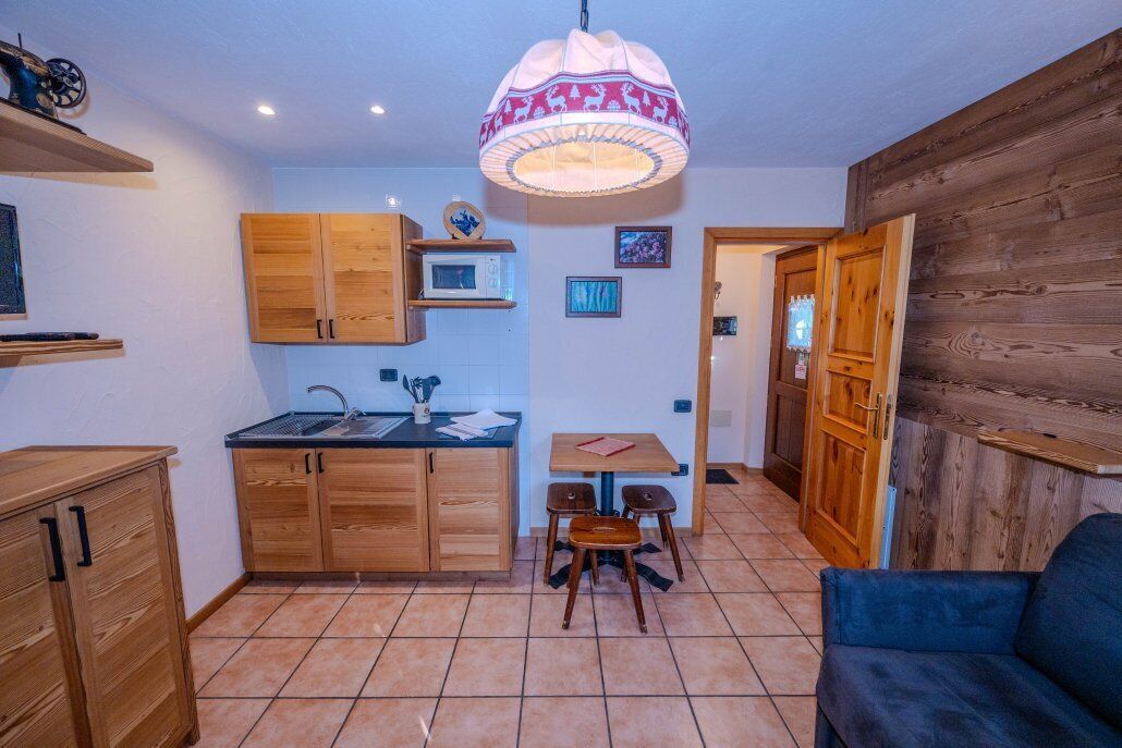 Cozinha compacta com armários de madeira, micro-ondas e luminária pendente.