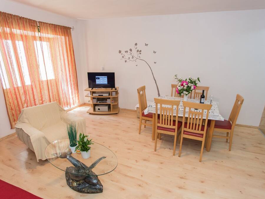 Sala de estar com televisão, mesa de jantar com cadeiras, sofá e uma escultura decorativa de peixe sobre uma mesa de vidro.