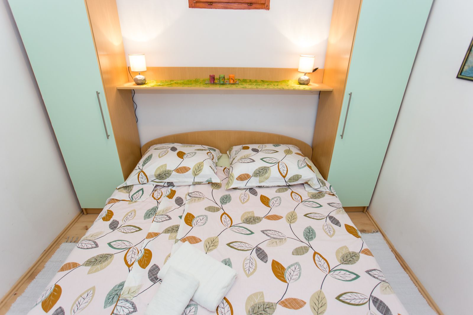 Um quarto pequeno e acolhedor, com uma cama, duas mesas de cabeceira com luminárias e uma prateleira sobre a cama.