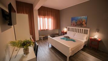 Um quarto com uma cama, mesa de cabeceira, televisão, janela com cortinas e um quadro na parede.