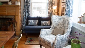 Uma sala de estar aconchegante com um sofá azul escuro, poltrona estampada e lareira de madeira.