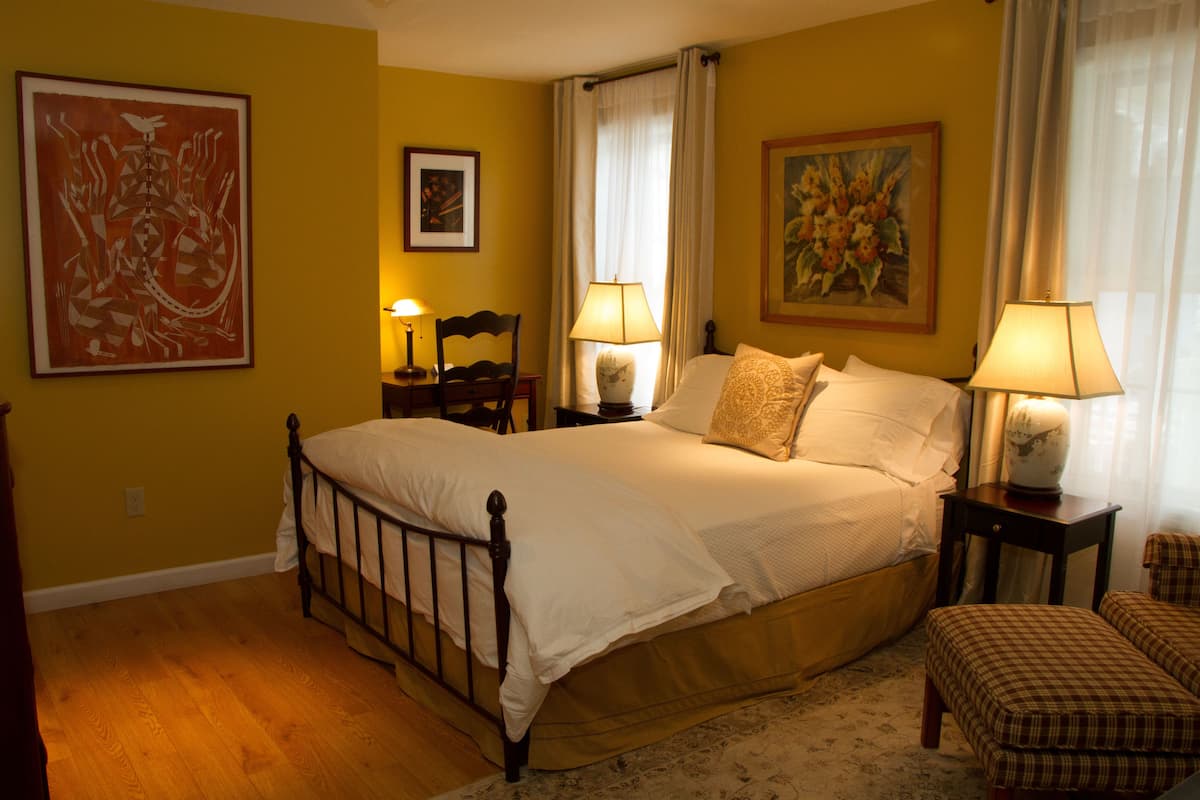 Um quarto com uma cama grande, duas mesas de cabeceira com abajures, uma cadeira e obras de arte nas paredes.