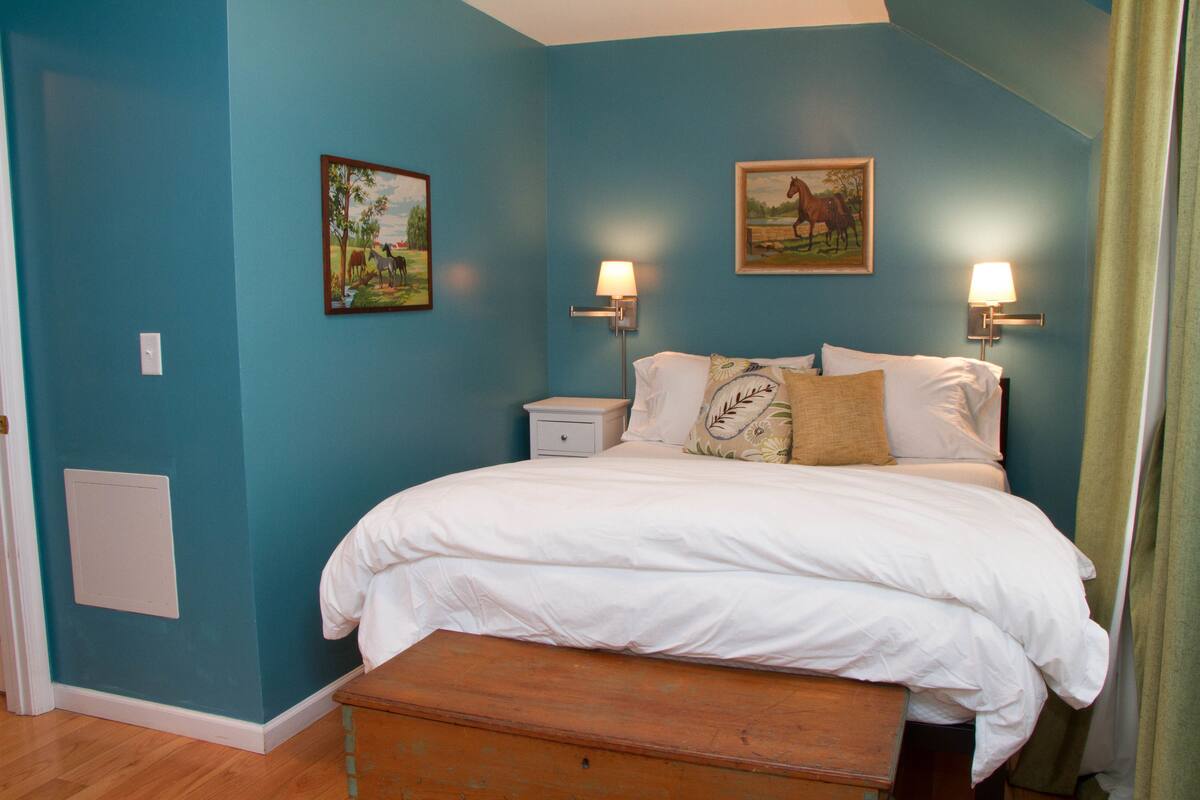 Quarto com cama, duas luminárias de parede, mesa de cabeceira e duas fotos emolduradas.