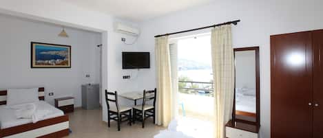 Quarto de hotel com cama, escrivaninha, cadeira, televisão, guarda-roupa e varanda com vista.