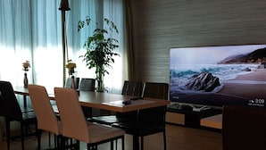 Uma área de refeições moderna com uma mesa e cadeiras de madeira, uma televisão de tela plana grande exibindo uma cena de praia e uma planta em vaso.