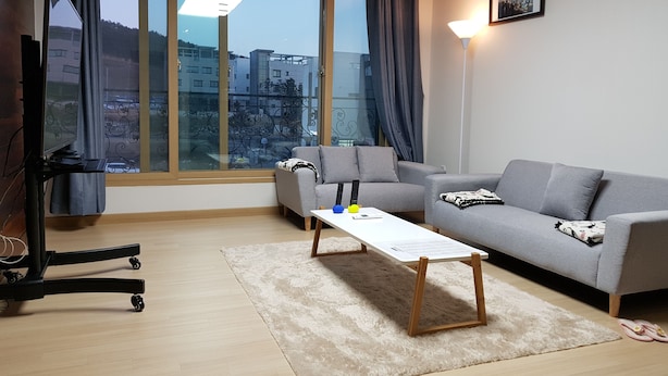 Uma sala de estar moderna com um sofá cinzento, uma mesa de centro branca e uma TV em um suporte.