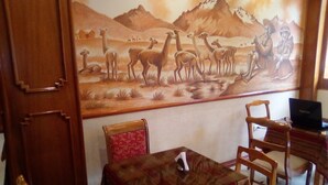 Uma área de refeições com mesa e cadeiras de madeira, um quadro com lhamas e montanhas na parede e um laptop sobre uma escrivaninha.