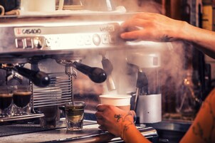 Uma pessoa operando uma máquina de expresso, com vapor saindo do porta-filtro.