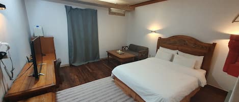 Quarto de hotel com cama, escrivaninha, cadeira, televisão e janela com cortinas.