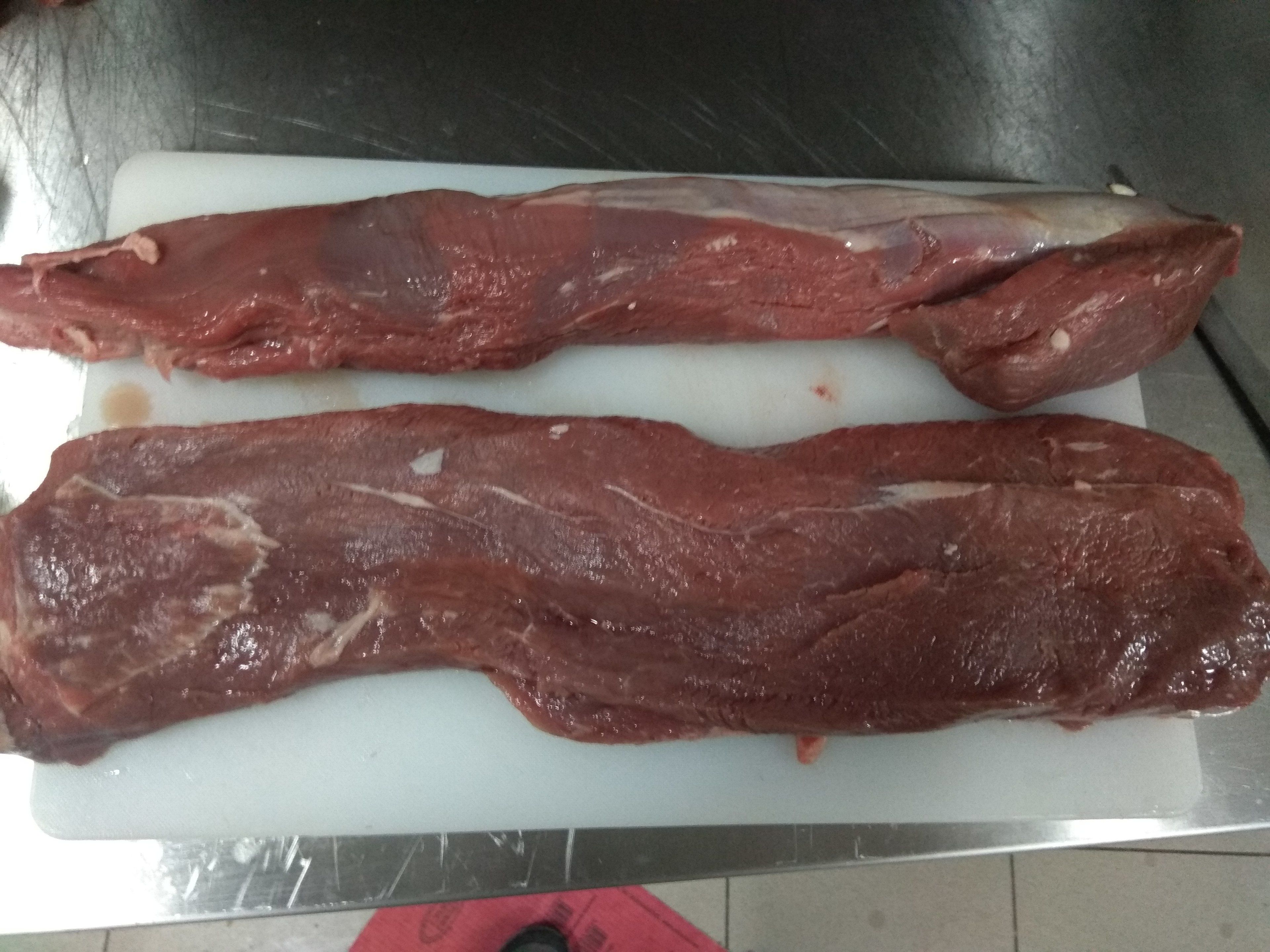 Dois pedaços de carne crua sobre uma tábua de corte branca.