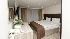 Quarto de hotel com cama, mesa de cabeceira, espelho e um vaso com flores.
