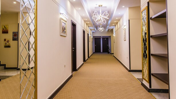Corredor de hotel com piso coberto de carpete, portas e luminária decorativa no teto.