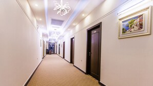 Um corredor de hotel com piso coberto por carpete, portas de madeira escura e um quadro emoldurado na parede.
