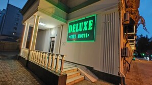 Um hotel chamado "Deluxe City Hotel" com um letreiro de neon, uma escadaria e uma varanda com guarda-corpo.