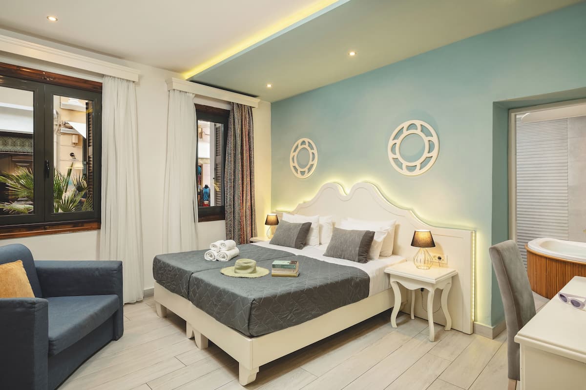 Quarto moderno com uma cama grande, mesas de cabeceira, uma cadeira, uma pequena mesa e uma janela com cortinas.