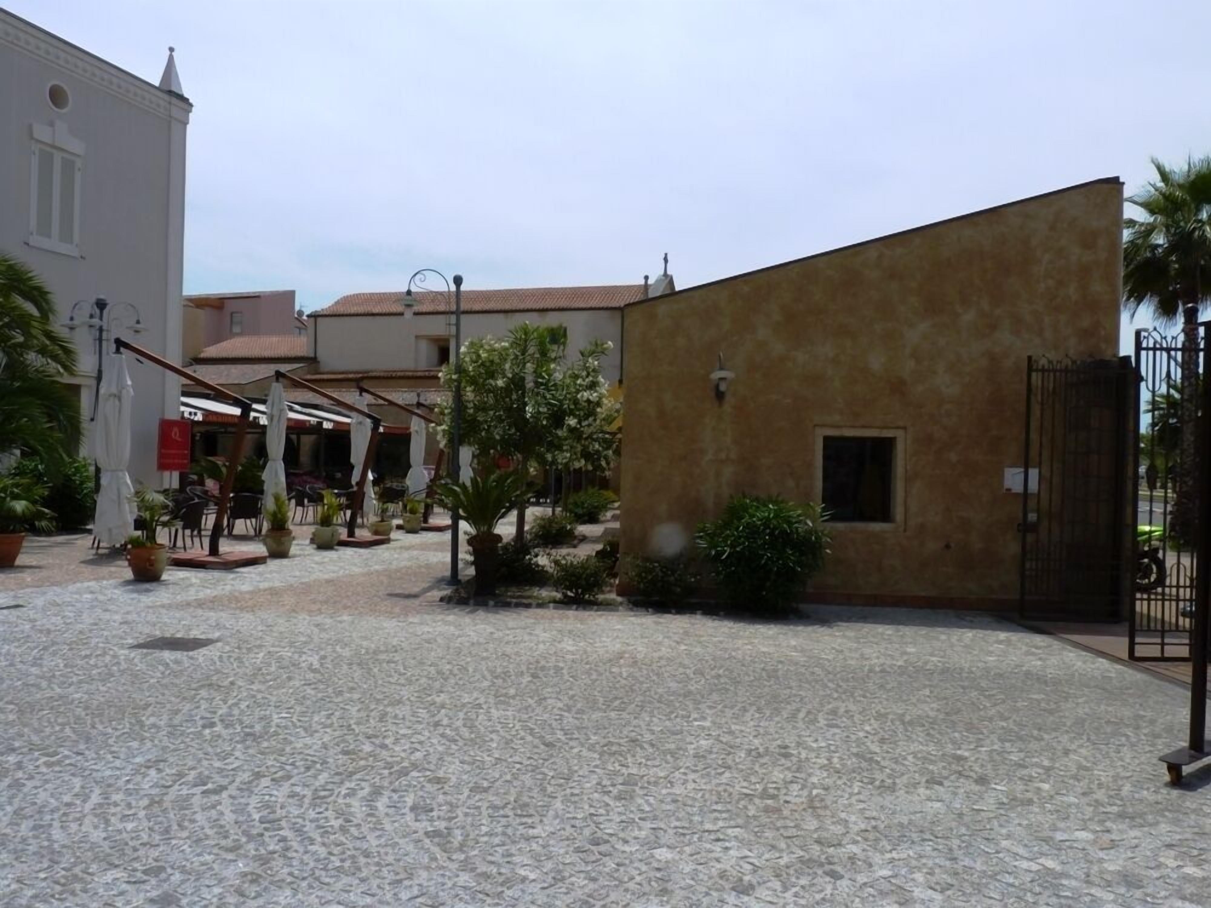 Um pátio com piso de pedras irregulares, um edifício com fachada bege e um portão.