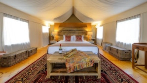 Um quarto espaçoso com tenda, uma cama grande, duas mesas de cabeceira com luminárias, um banco de madeira e um tapete estampado.