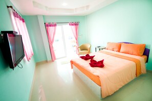 Quarto com cama, uma cadeira, uma televisão e janela com cortinas.