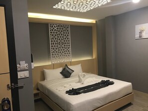 Quarto de hotel moderno, com cama bem arrumada, cabeceira decorativa e luminária fixada na parede.
