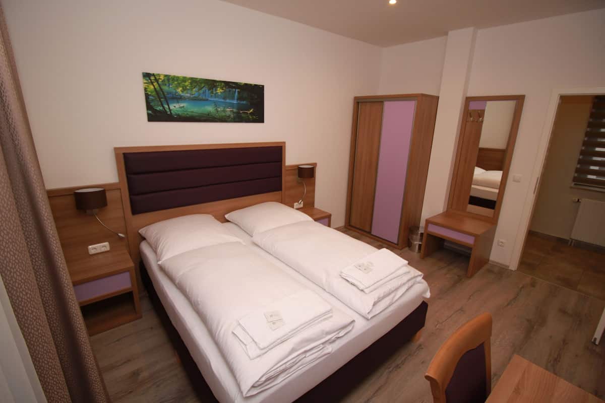 Quarto de hotel com uma cama grande, mesas de cabeceira, um guarda-roupa, um espelho e um quadro na parede.