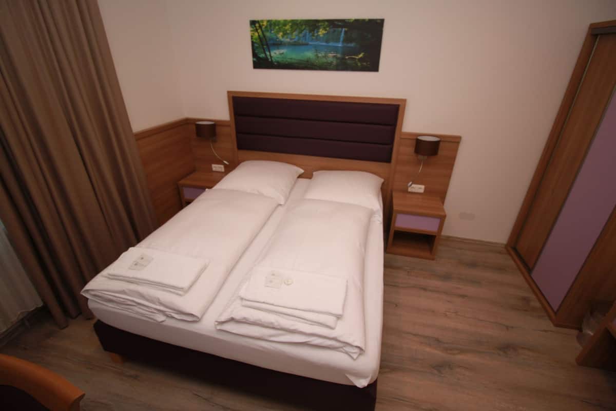 Uma cama de casal com cabeceira de madeira, duas mesas de cabeceira e um quadro na parede.