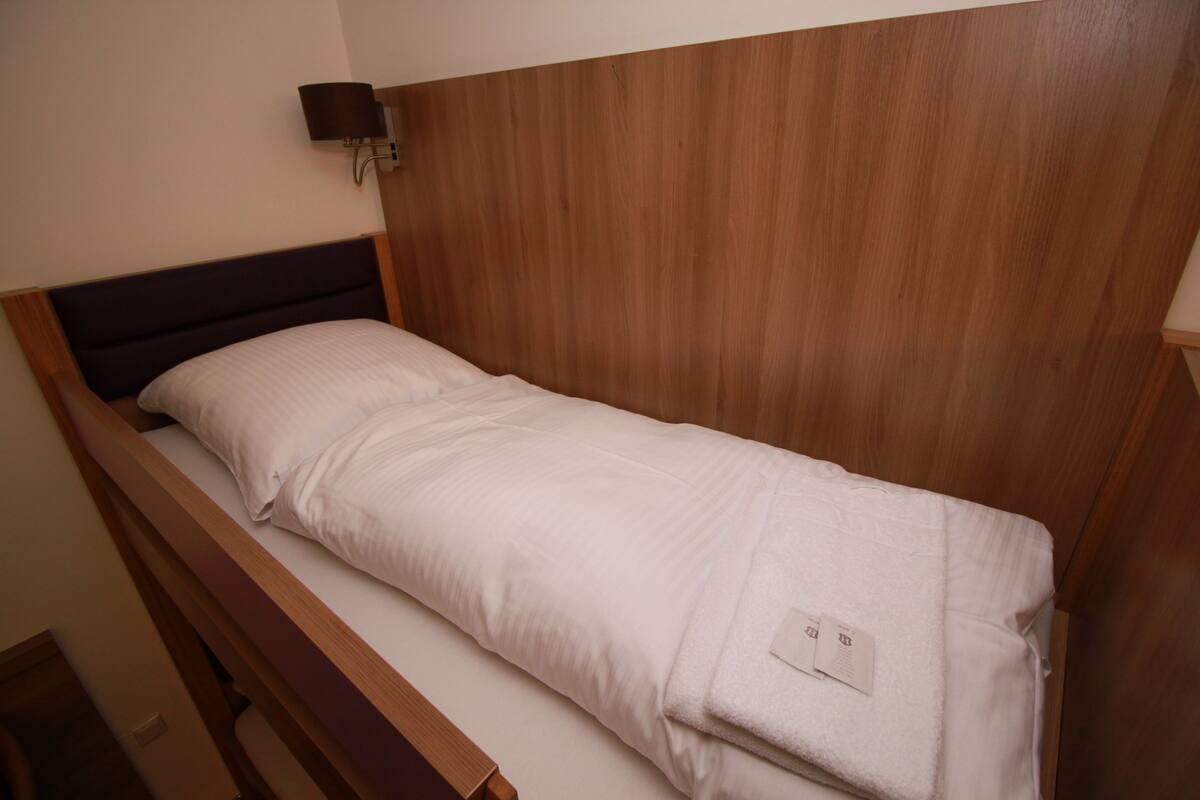 Uma cama de solteiro com cabeceira de madeira e uma luminária fixada na parede.