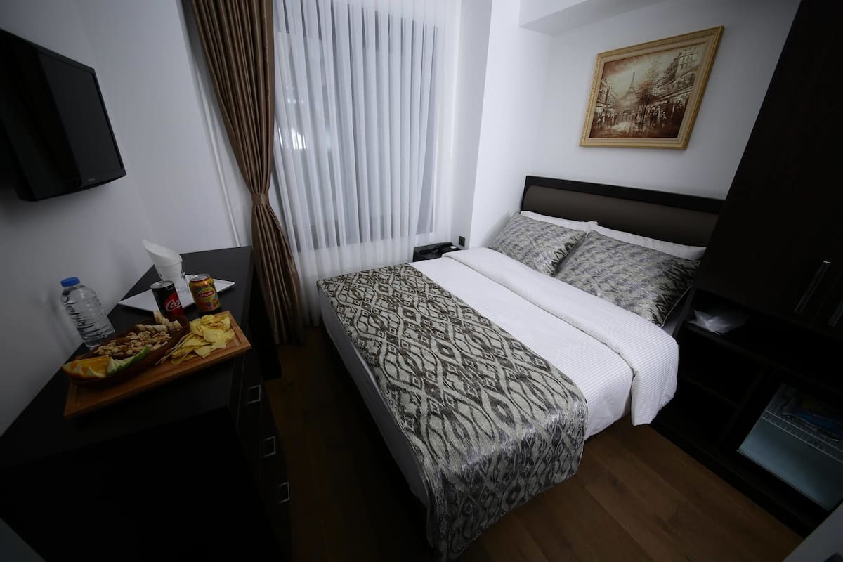 Quarto de hotel com uma cama, televisão, quadro e bandeja de café da manhã sobre uma mesa.