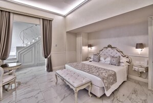 Um quarto espaçoso com uma cama grande, um banco, uma mesa de cabeceira e vista para uma escadaria.