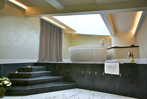 Uma casa de banho moderna com uma banheira grande, degraus de mármore e um claraboia.