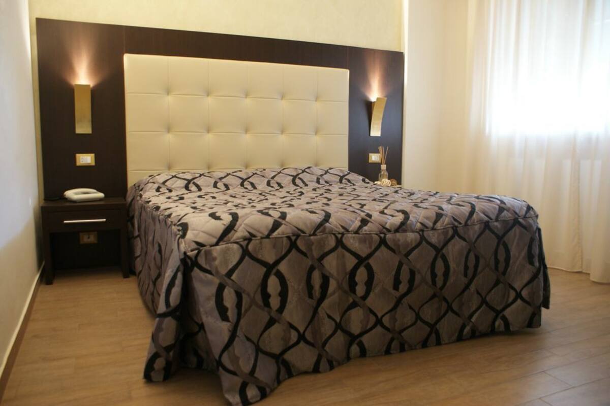 Quarto com cabeceira estofada, colcha estampada, abajures e mesa de cabeceira.